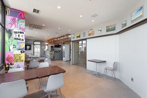 Uma área de jantar moderna com uma mesa de madeira e cadeiras brancas, uma cozinha ao fundo e uma parede com quadros.