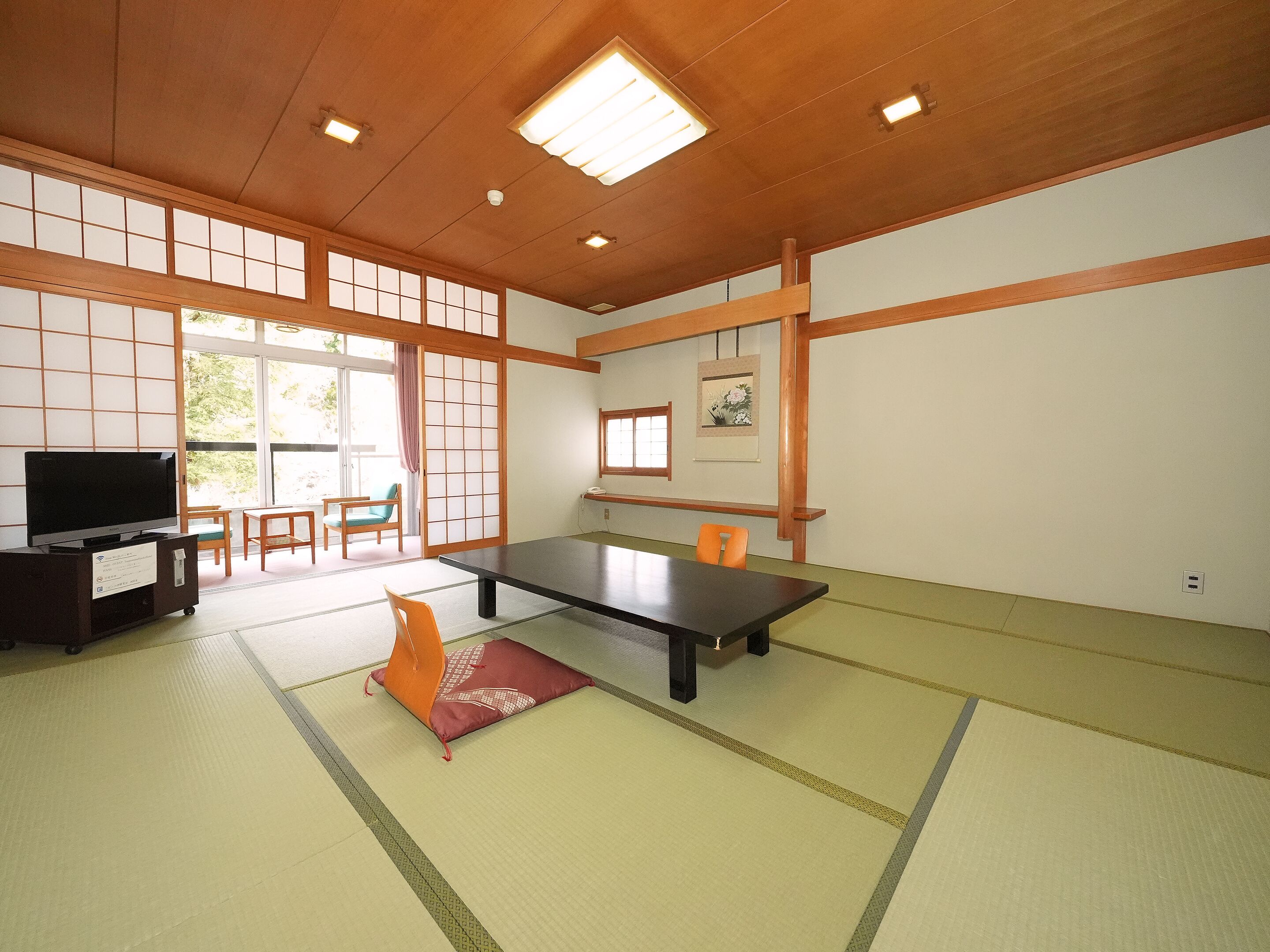 Quarto em estilo japonês tradicional com tatames, uma mesa baixa, televisão e portas deslizantes.