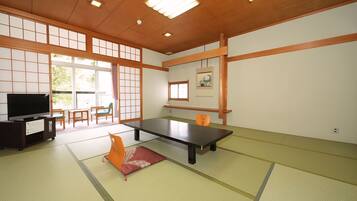 Quarto em estilo japonês tradicional com tatames, uma mesa baixa, televisão e portas deslizantes.