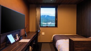 Quarto de hotel com uma televisão de tela grande, uma escrivaninha com luminária, uma cama e uma janela com vista para as montanhas.