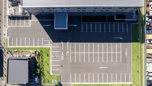 Vista aérea de um estacionamento com vagas demarcadas, uma passarela para pedestres e um edifício com várias janelas.