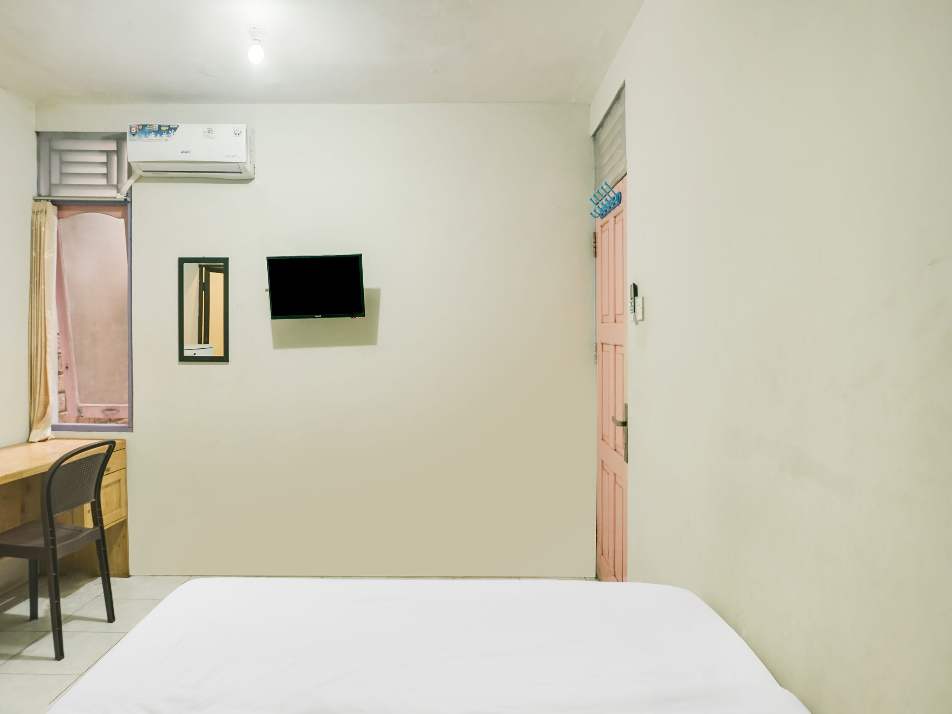 Quarto com cama, escrivaninha, cadeira, ar-condicionado, televisão e porta.