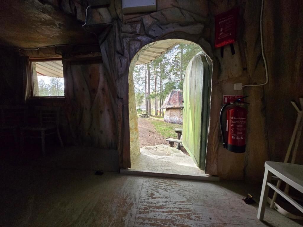 Interior rústico de madeira com uma porta que dá para o exterior, um extintor de incêndio na parede e um banco.