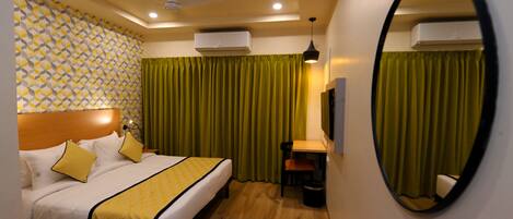 Quarto de hotel com cama, escrivaninha, cadeira, espelho e ar condicionado.