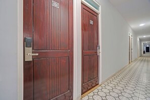 Um corredor com duas portas de madeira, cada uma com um número. O chão tem um padrão de azulejos.