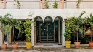 Entrada de edifício com fachada azulejada, portas de vidro e plantas em vasos.