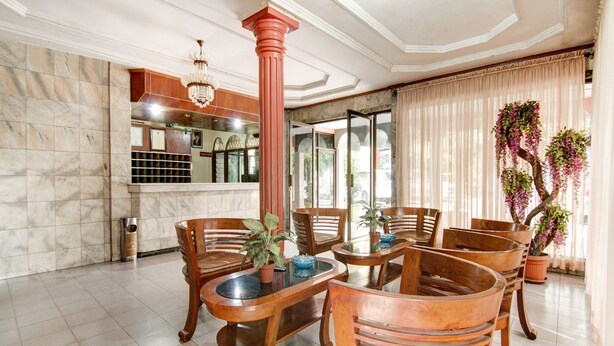 Um hall amplo com piso de mármore, mobiliário de madeira e grandes janelas com cortinas.