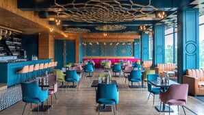 Um restaurante moderno com diversas opções de assentos, incluindo mesas e cabines, e um bar com balcão de madeira.