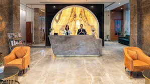 Uma área de recepção com um balcão de mármore, dois poltronas laranja e um grande mural na parede.