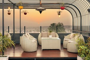 Um terraço com área de estar, móveis de vime, vasos pendurados e vista panorâmica da cidade.