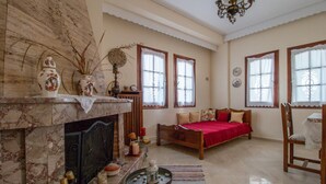 Uma sala de estar ampla com lareira, cama com colcha vermelha e janelas grandes.