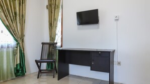 Quarto com escrivaninha, cadeira e televisão presa na parede.