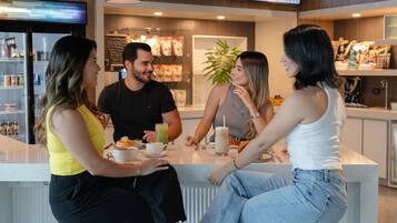 Um grupo de pessoas sentado ao balcão de um café, com um quadro de menu e uma televisão ao fundo.