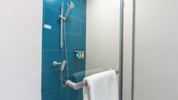 Chuveiro com porta de vidro, toalha branca pendurada em barra de toalhas e produtos de higiene em uma prateleira.