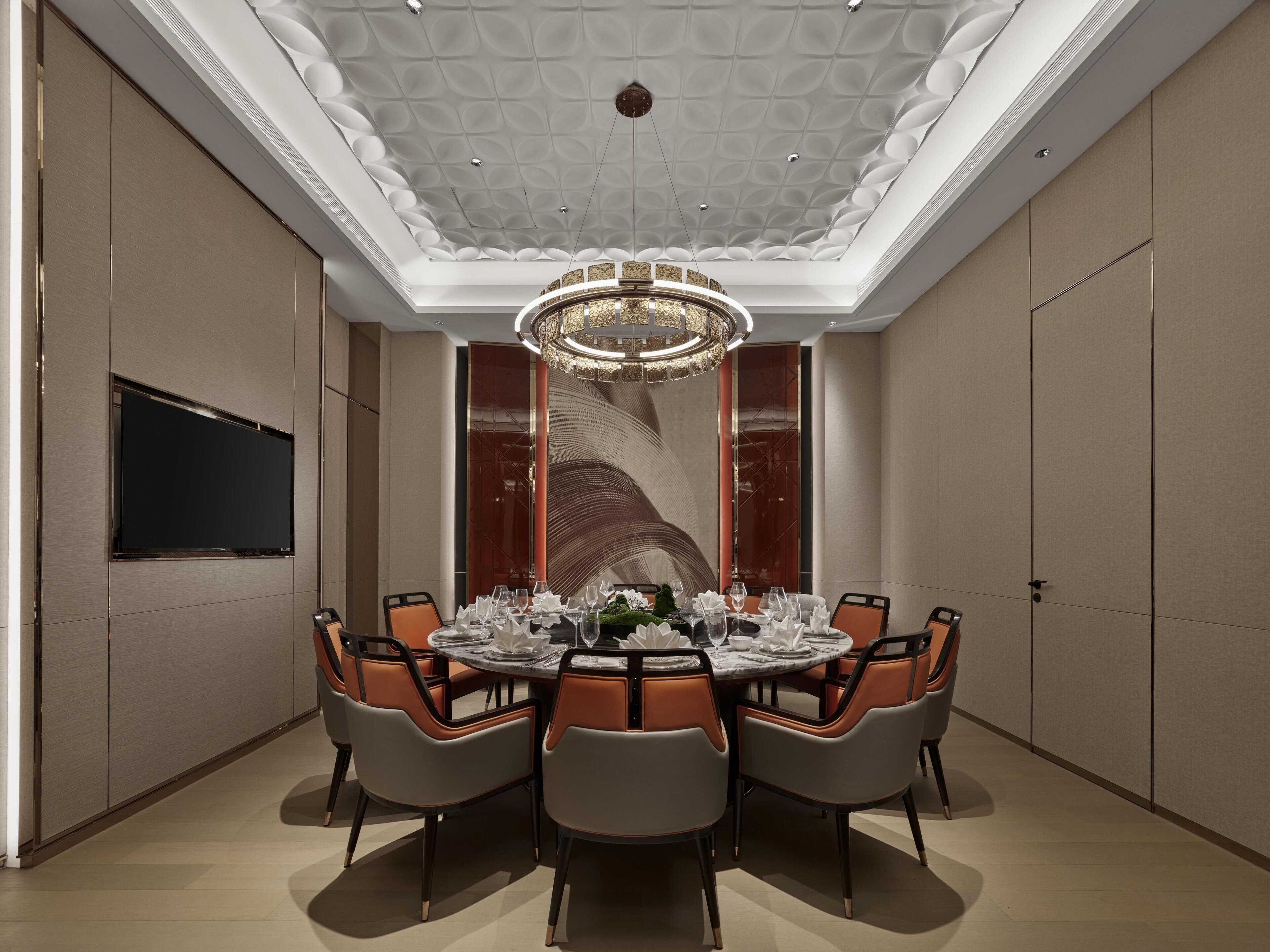 Uma sala de jantar moderna com uma mesa redonda, seis cadeiras, um candelabro e uma televisão de parede grande.