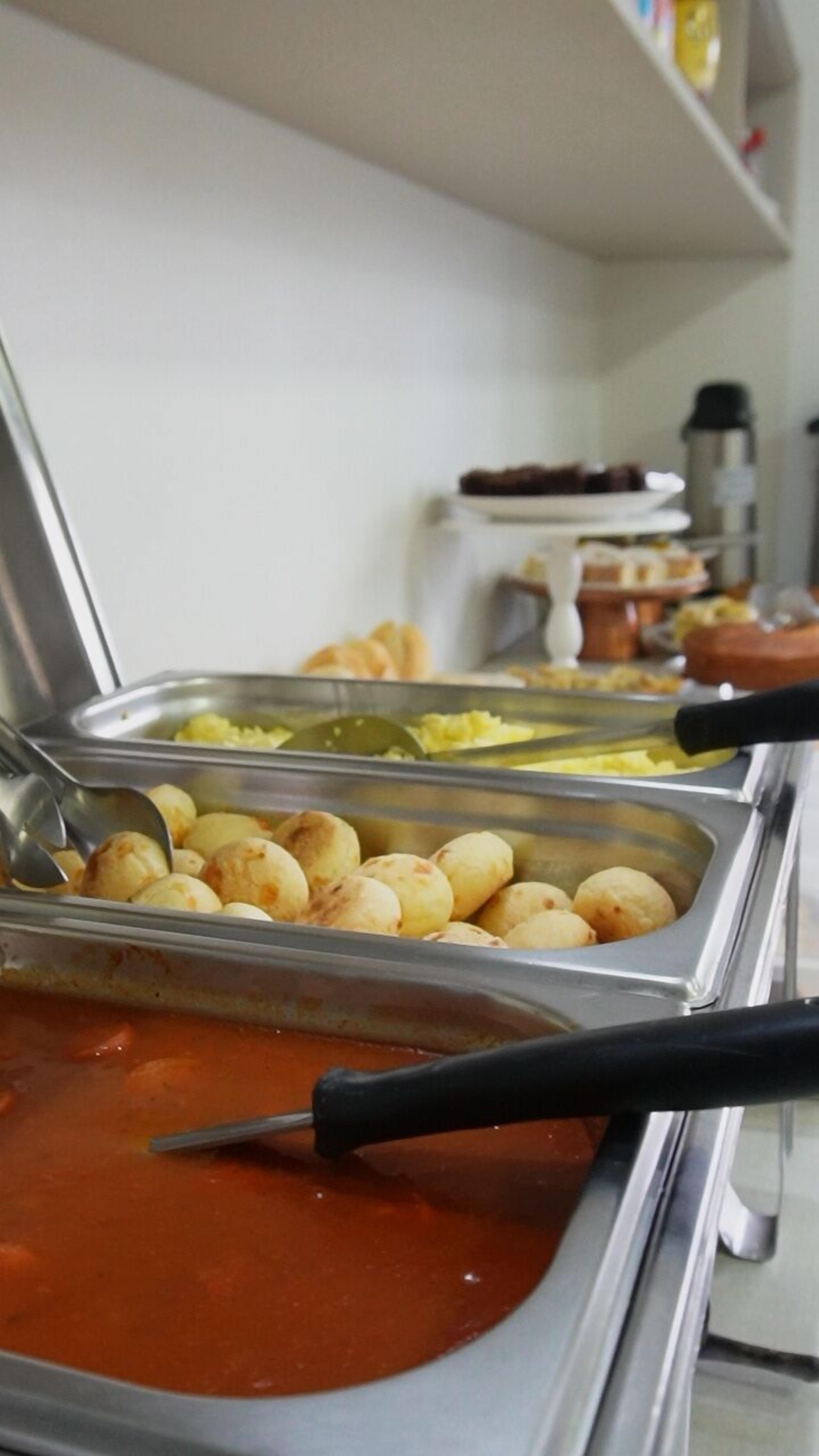 Buffet com diversos alimentos, incluindo sopa à base de tomate, ovos cozidos e outros pratos em recipientes de metal.