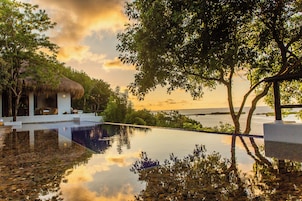 Piscina infinita refletindo árvores e um pôr do sol.