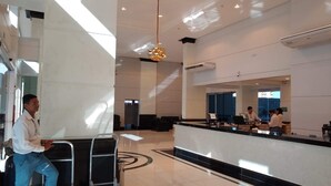 Um hall amplo com balcão de recepção, área de espera com cadeiras e um lustre moderno.