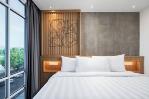 Quarto de hotel moderno com uma cama grande, cabeceira de madeira e vista para a cidade pela janela.