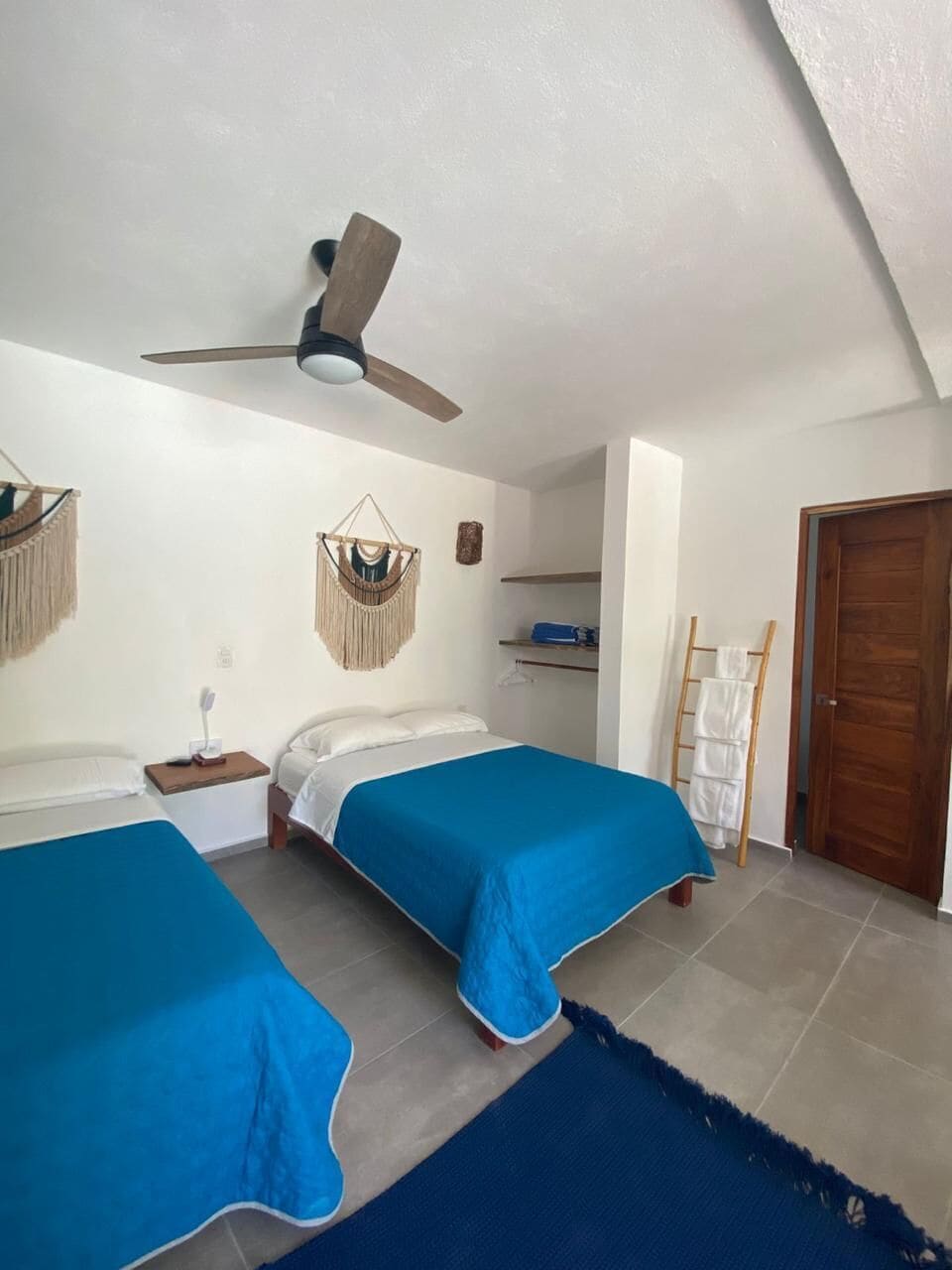 Quarto com duas camas, um ventilador de teto, uma escada de madeira e uma porta branca.