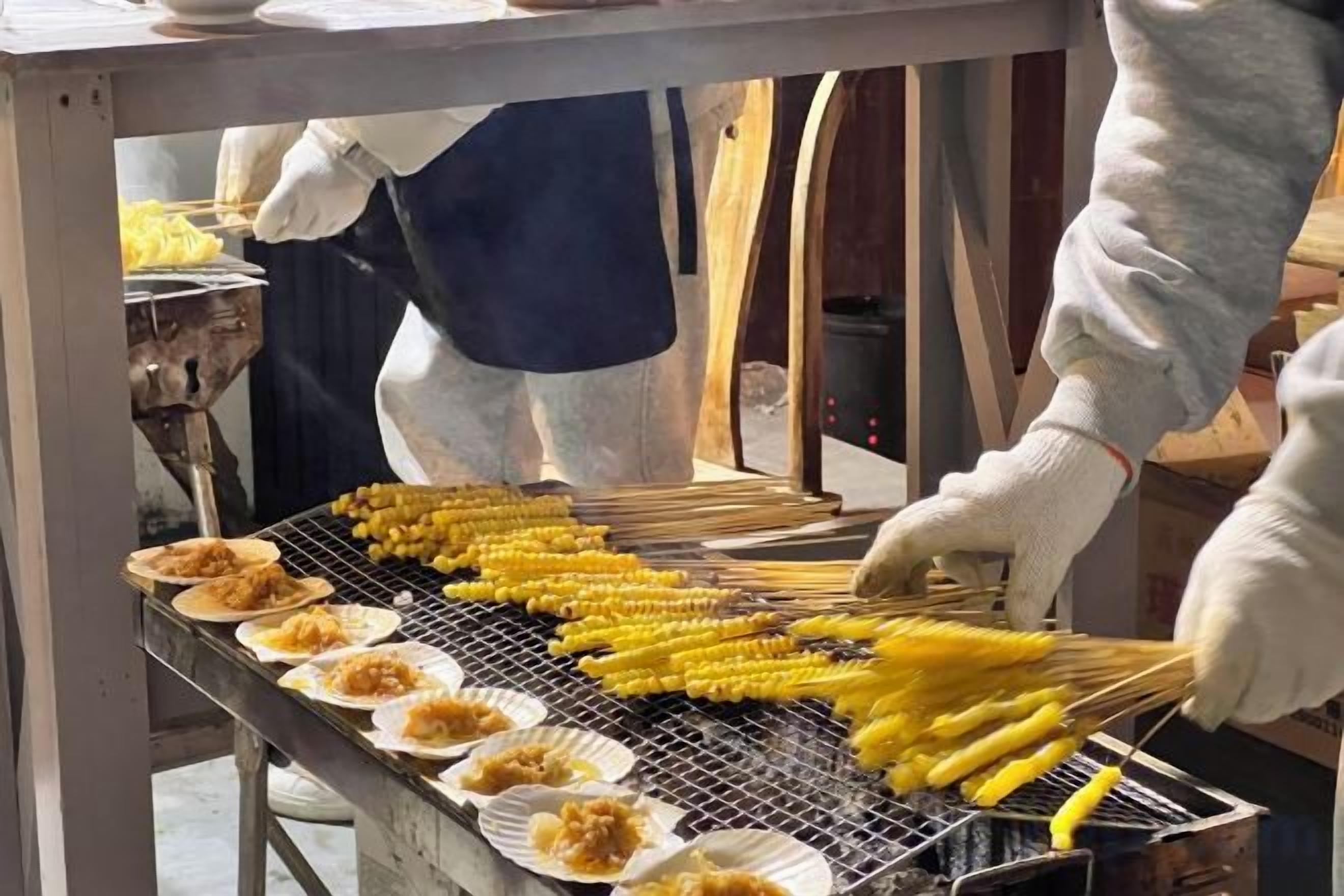 Espaço para preparação de alimentos com churrasqueira, milho e pratos de papel.