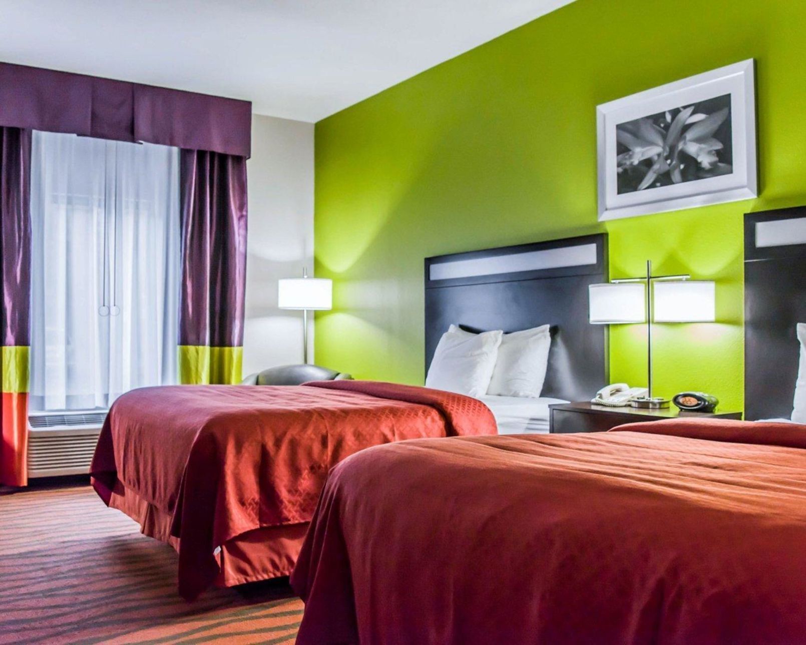 Quarto de hotel com duas camas, uma janela grande com cortinas, uma parede verde e um quadro na parede.