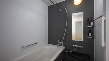 Um banheiro moderno com uma banheira branca, chuveiro com mangueira e espelho fixado na parede, além de um nicho com produtos de higiene pessoal.
