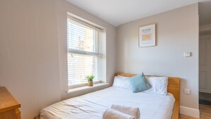 Uma cama bem arrumada com lençóis brancos, cabeceira de madeira e uma janela com persianas.