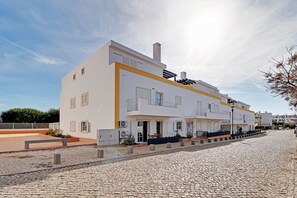 Um edifício moderno com fachada branca e detalhes amarelos, com varandas e rua de paralelepípedos.
