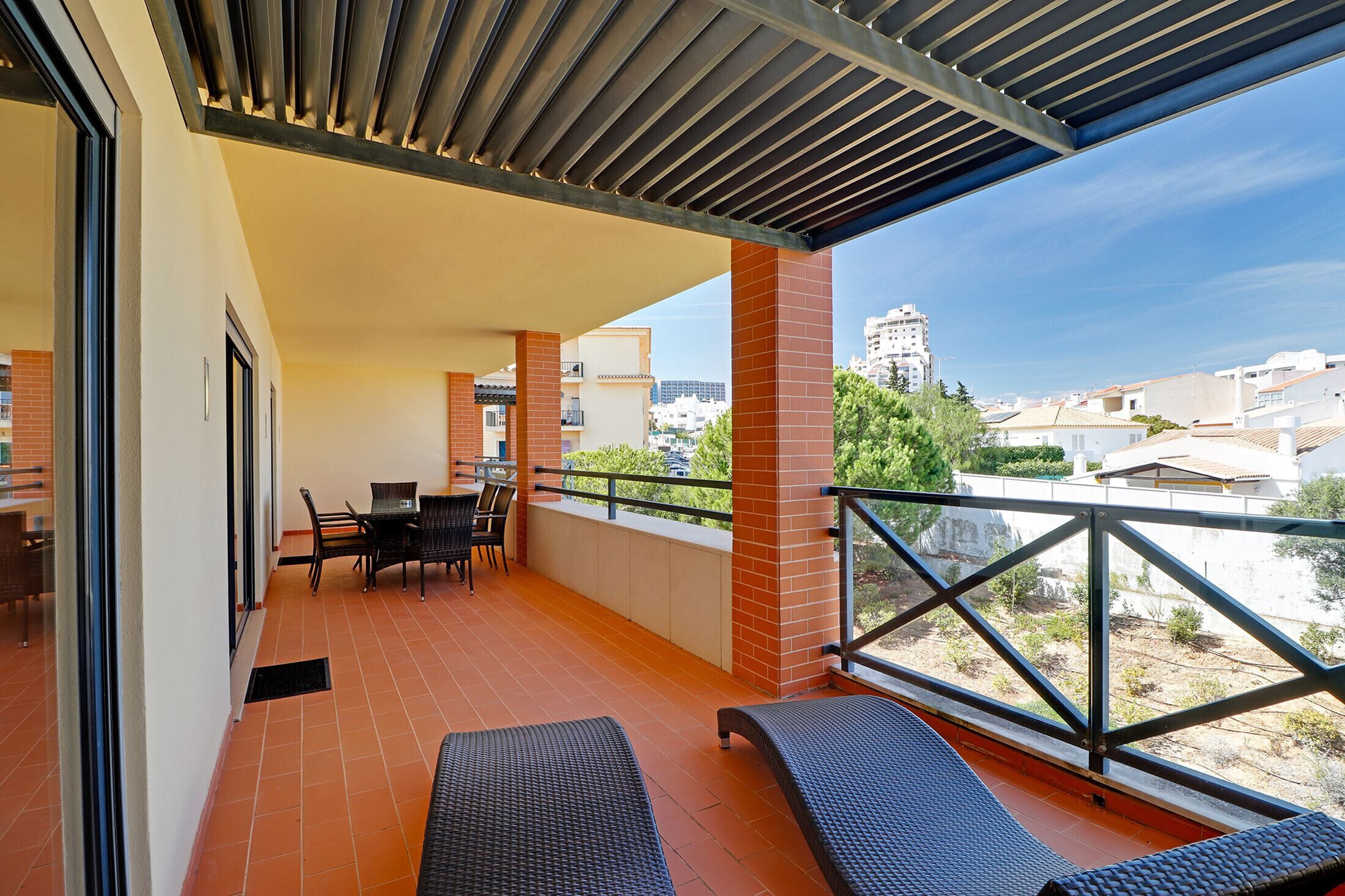Uma varanda com mesa e cadeiras, vista da cidade e um prédio ao fundo.