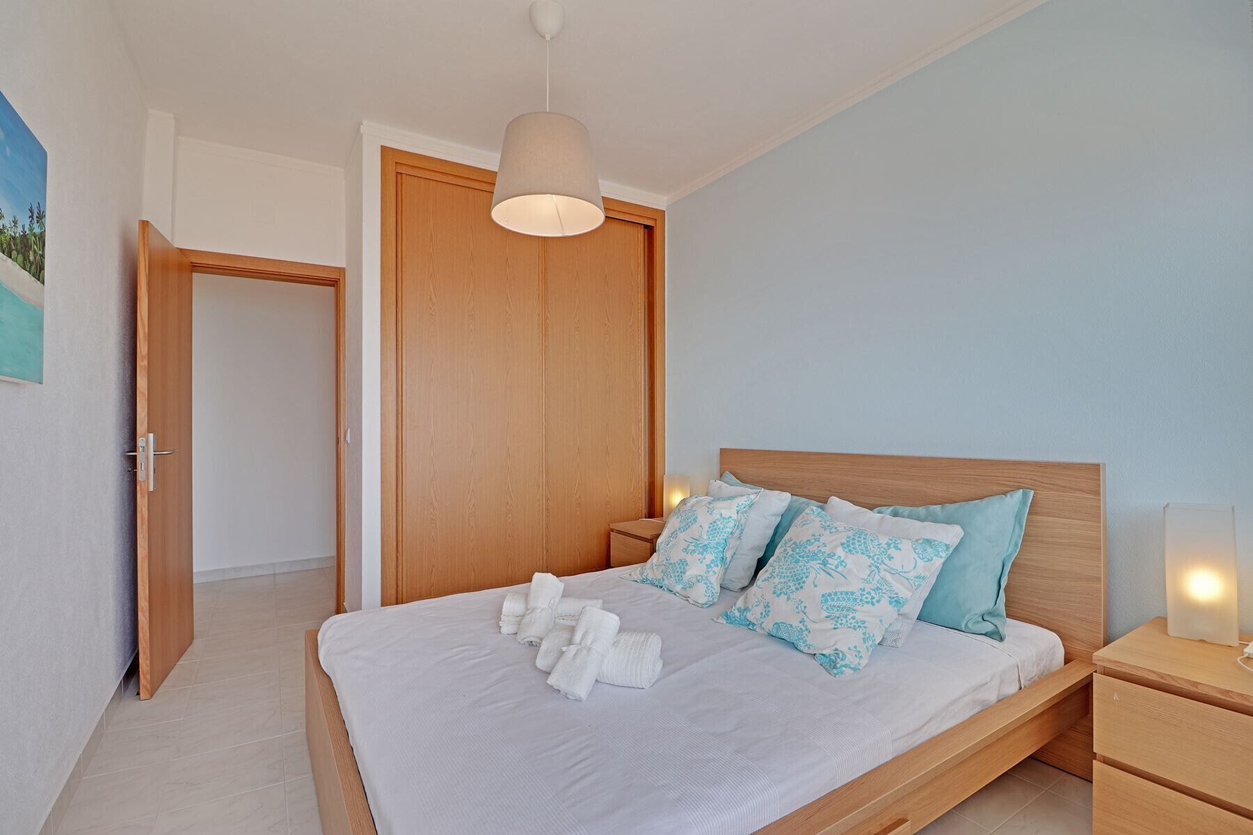 Quarto com cama, cabeceira de madeira e mesa de cabeceira com abajur.