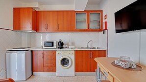 Cozinha compacta com armários de madeira, micro-ondas, máquina de lavar e um pequeno frigorífico.