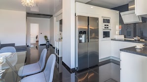 Uma cozinha moderna com eletrodomésticos de aço inoxidável, uma área de jantar com mesa de vidro e um candelabro.