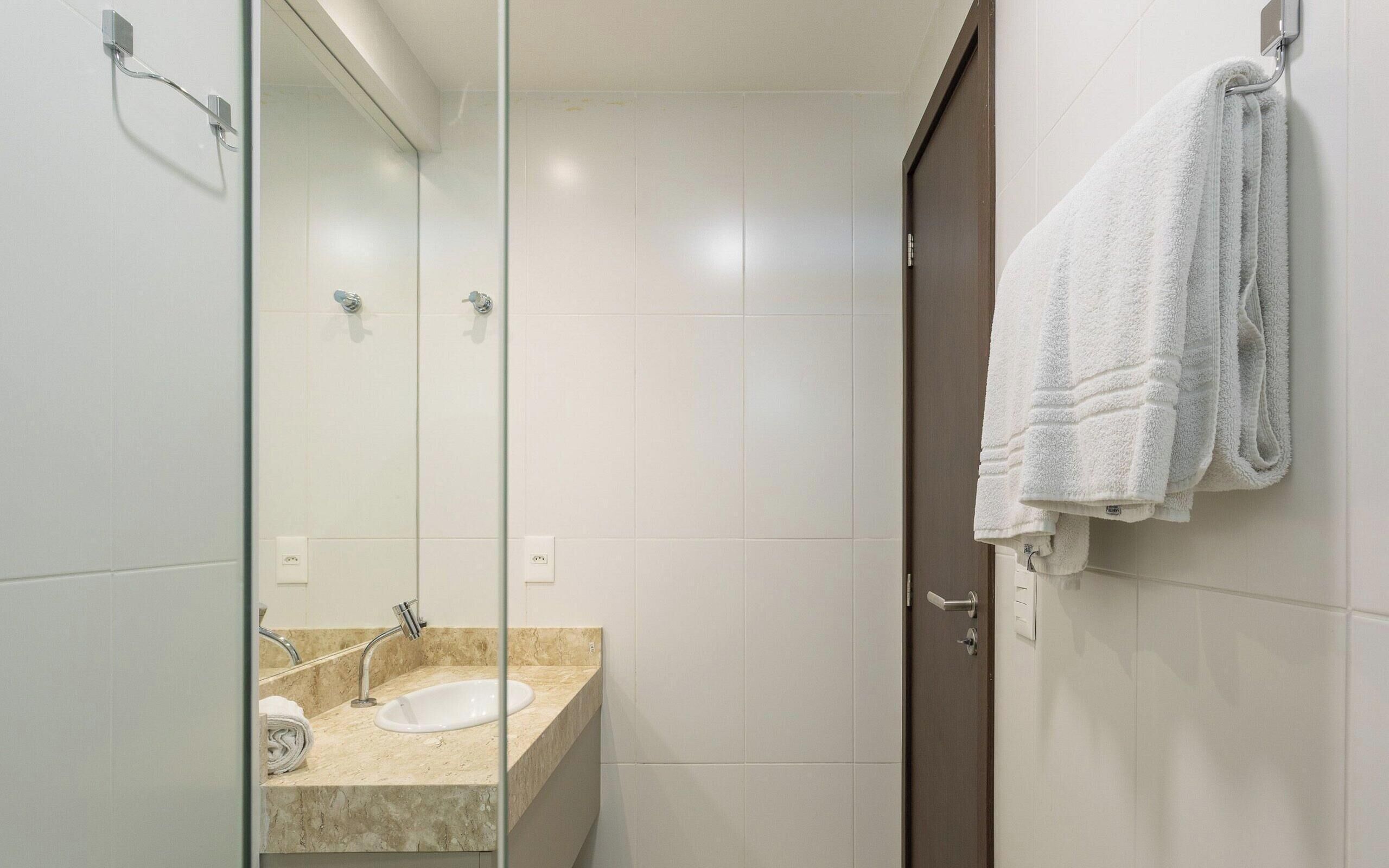 Casa de banho com cabine de duche em vidro, lavatório com bancada de mármore e toalha pendurada num suporte fixado na parede.