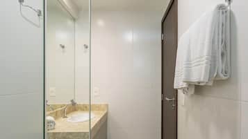 Casa de banho com cabine de duche em vidro, lavatório com bancada de mármore e toalha pendurada num suporte fixado na parede.