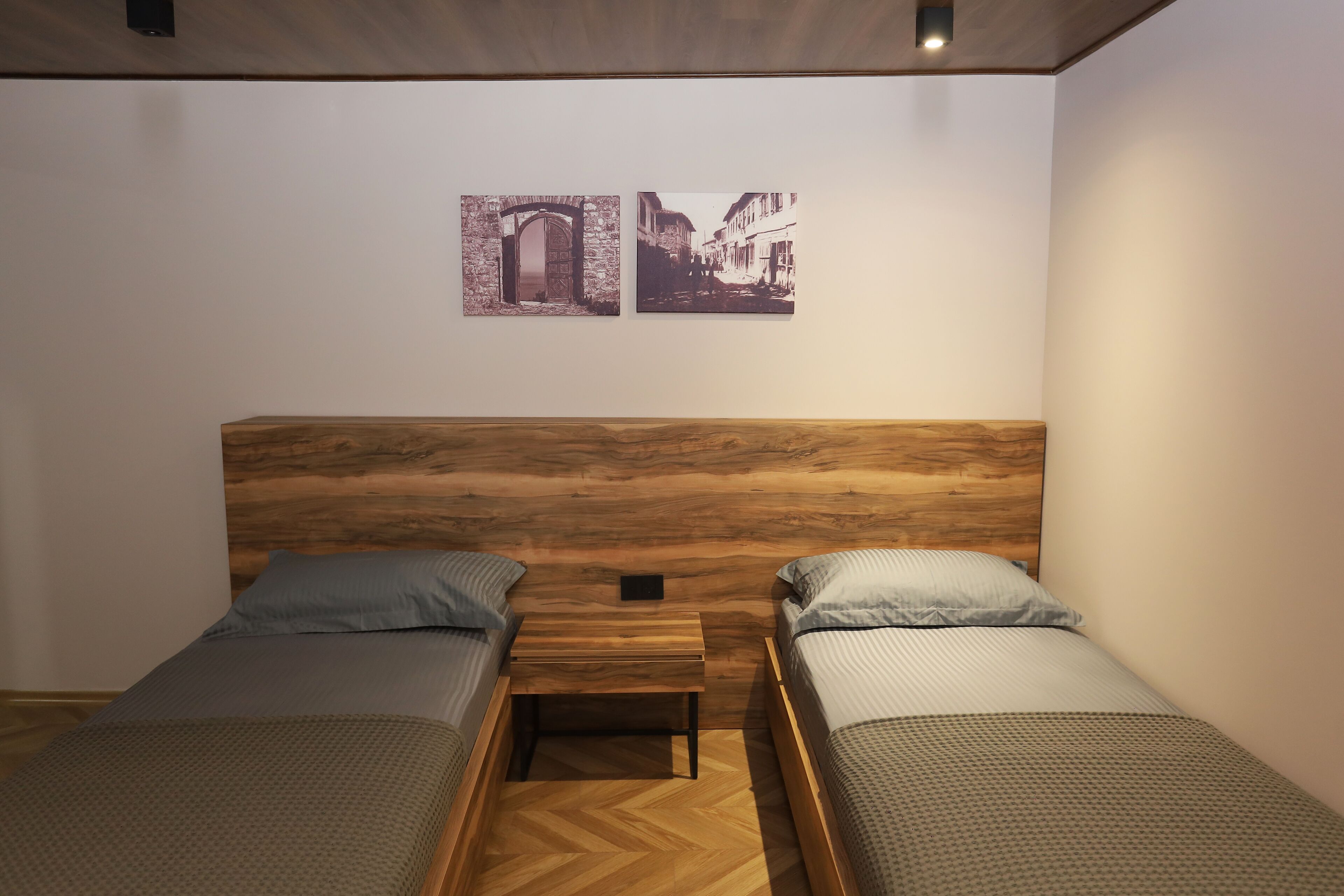 Quarto com duas camas de solteiro, cabeceira de madeira, mesa de cabeceira e duas quadros na parede.