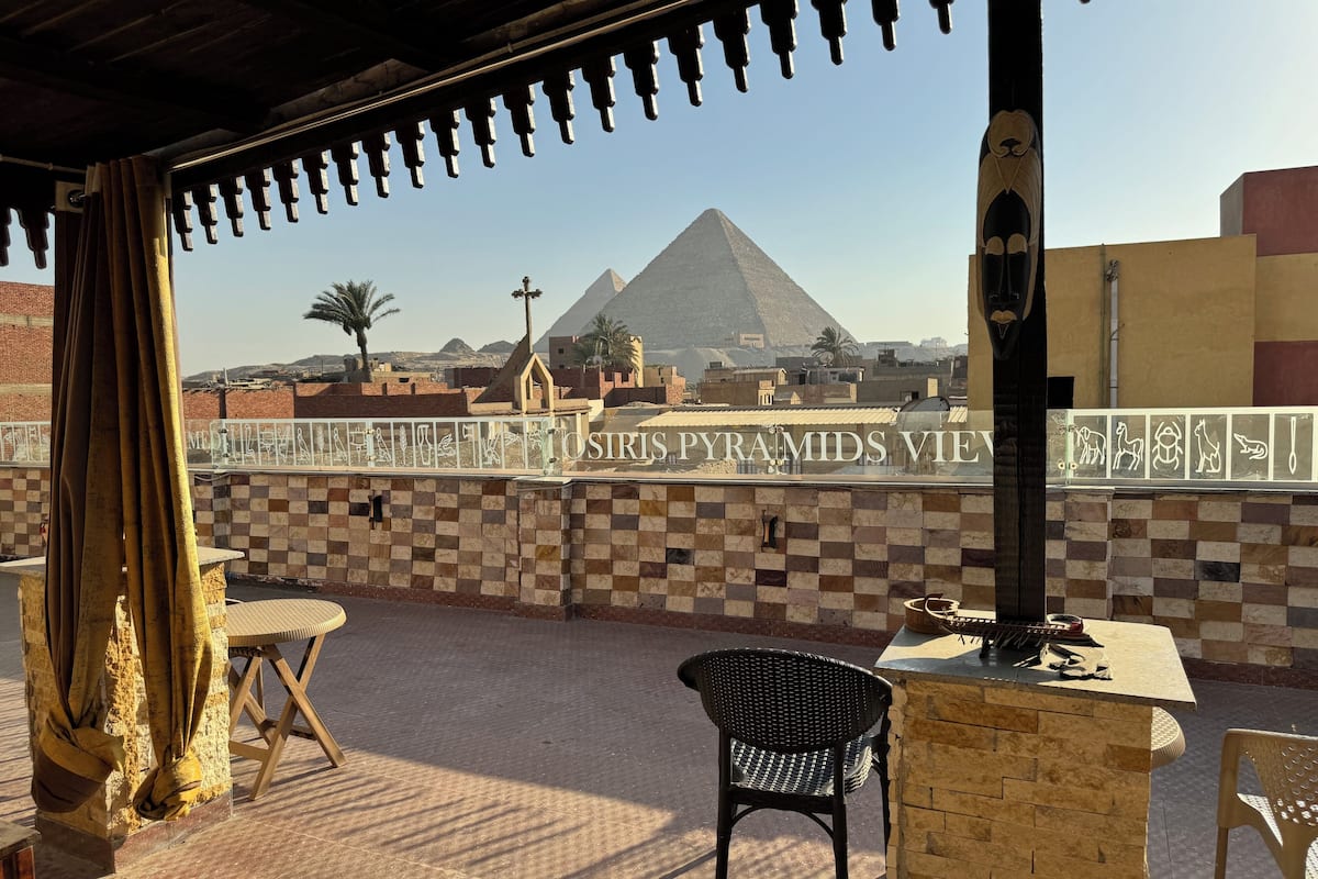 Um terraço com vista para as pirâmides, com uma parede xadrez, uma mesa e uma cadeira.