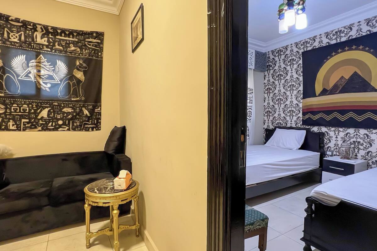 Quarto de hotel com cama, sofá, uma mesinha e um tapeçário na parede.