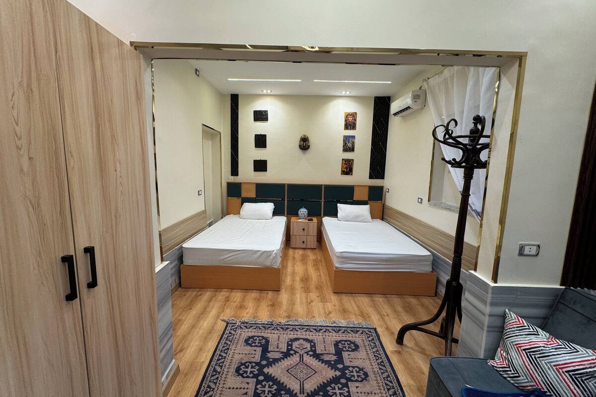 Quarto com duas camas, um guarda-roupa de madeira, um abajur e um tapete estampado.