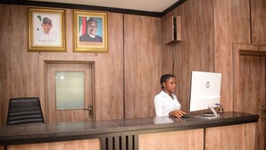 Uma receção com retratos emoldurados acima, um monitor de computador e uma cadeira de escritório preta.