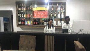 Uma área de bar com prateleiras cheias de garrafas de bebidas e um balcão com dois funcionários.