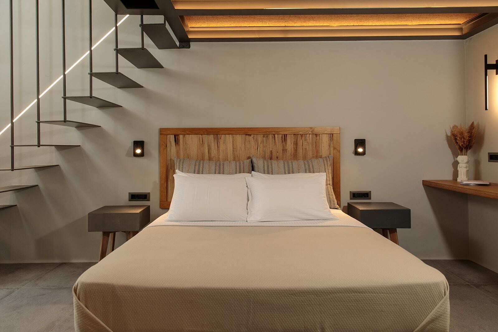 Quarto moderno com cama, cabeceira de madeira, mesas de cabeceira, luminária na parede e uma escada.