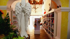 Um corredor com estátua de anjo branco, escada e prateleiras com diversos objetos.