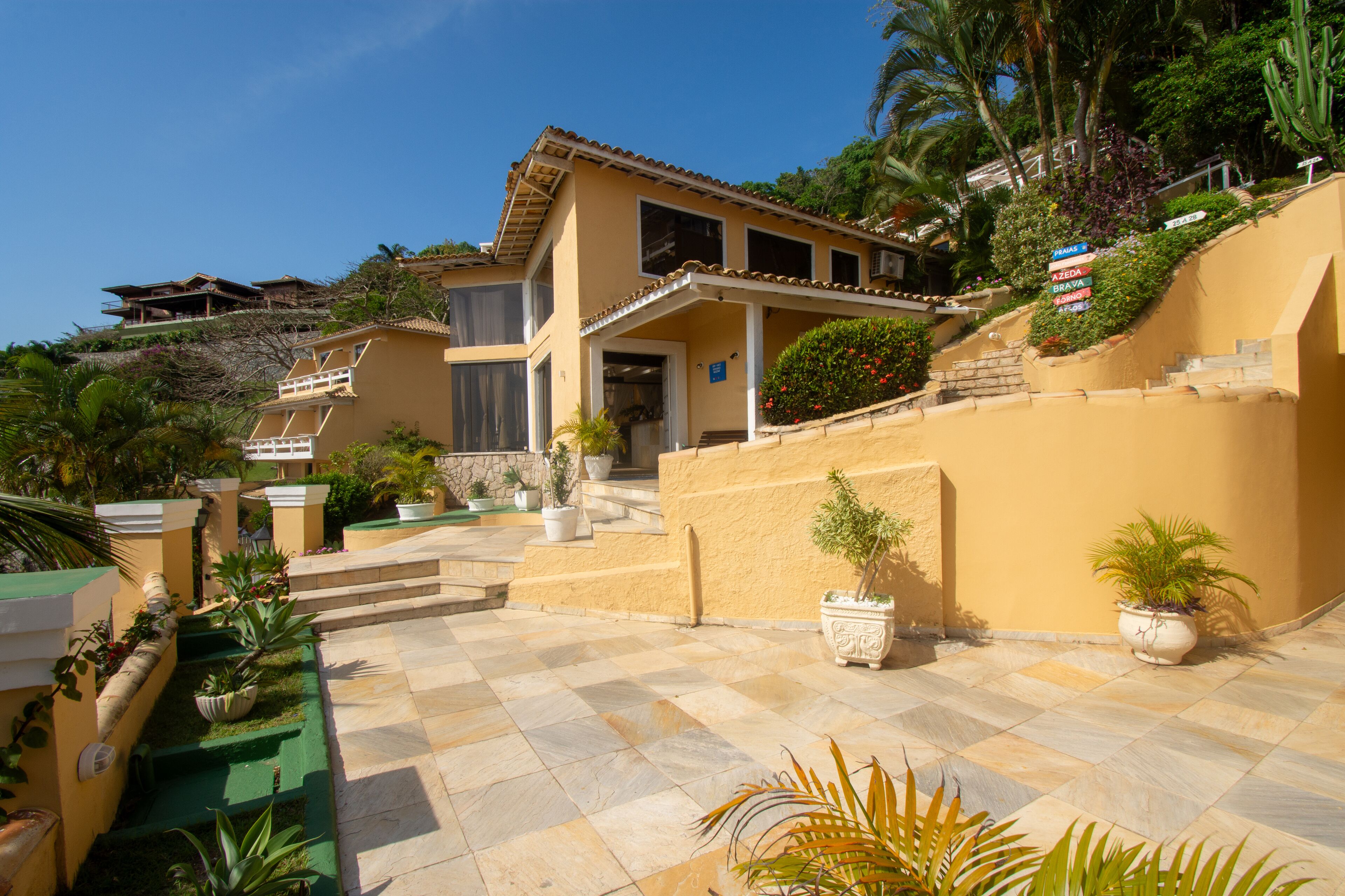 Uma casa de vários andares com um pátio ladrilhado, plantas em vasos e uma escadaria que leva à entrada.