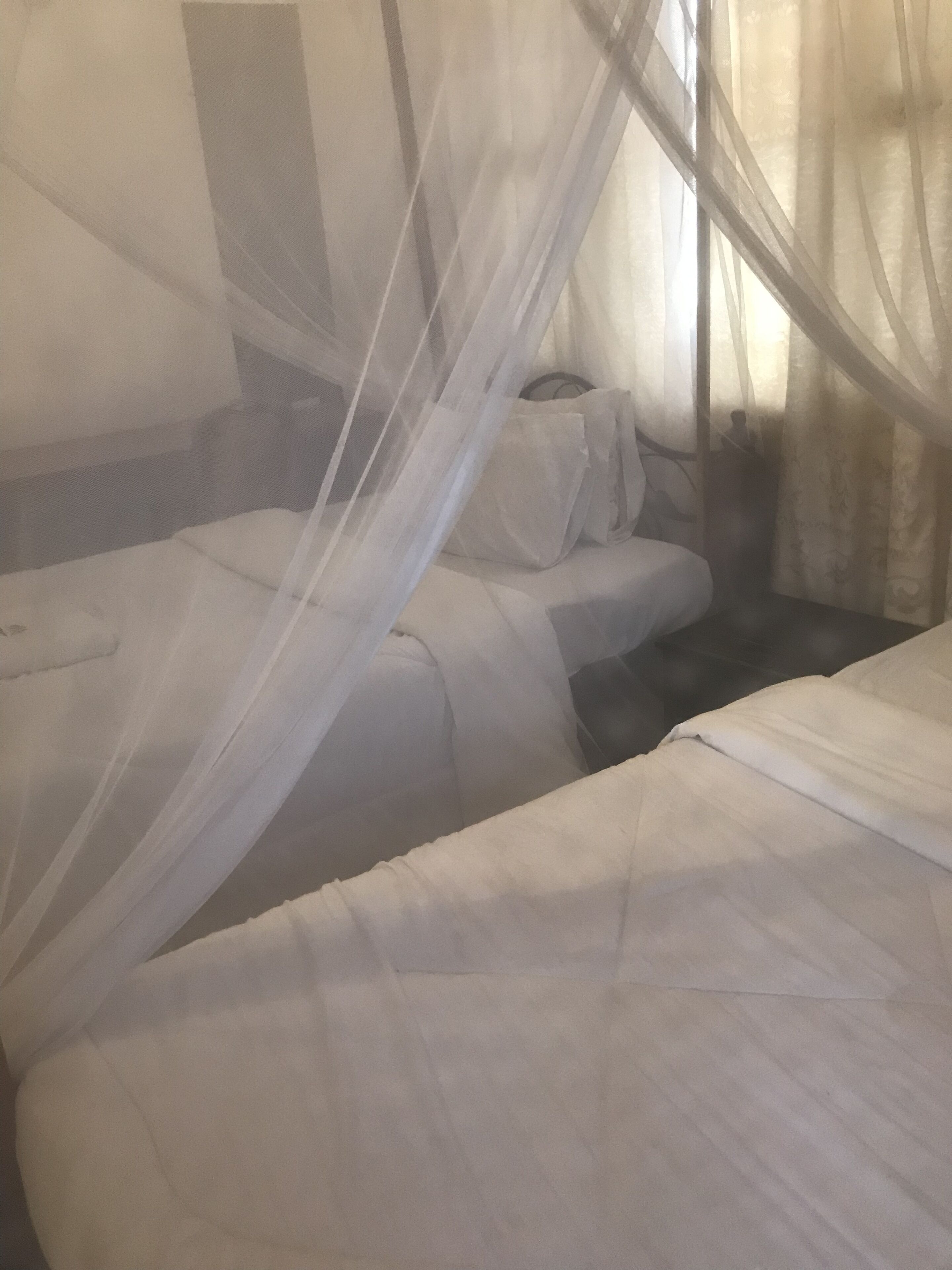 Quarto com duas camas, mosquiteiro e janela com cortinas.