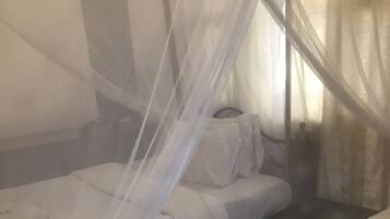 Quarto com duas camas, mosquiteiro e janela com cortinas.