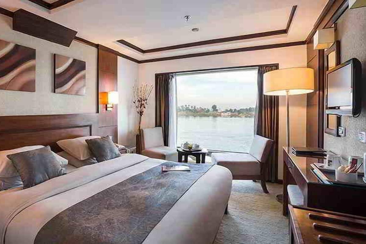 Quarto de hotel com uma cama grande, escrivaninha, cadeira e vista para um corpo de água.