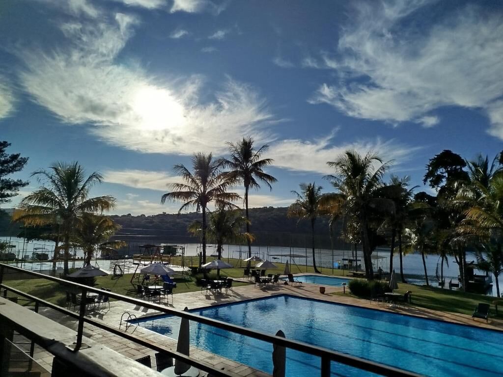 Piscina com espreguiçadeiras e guarda-sóis, cercada por palmeiras e vista para a água.