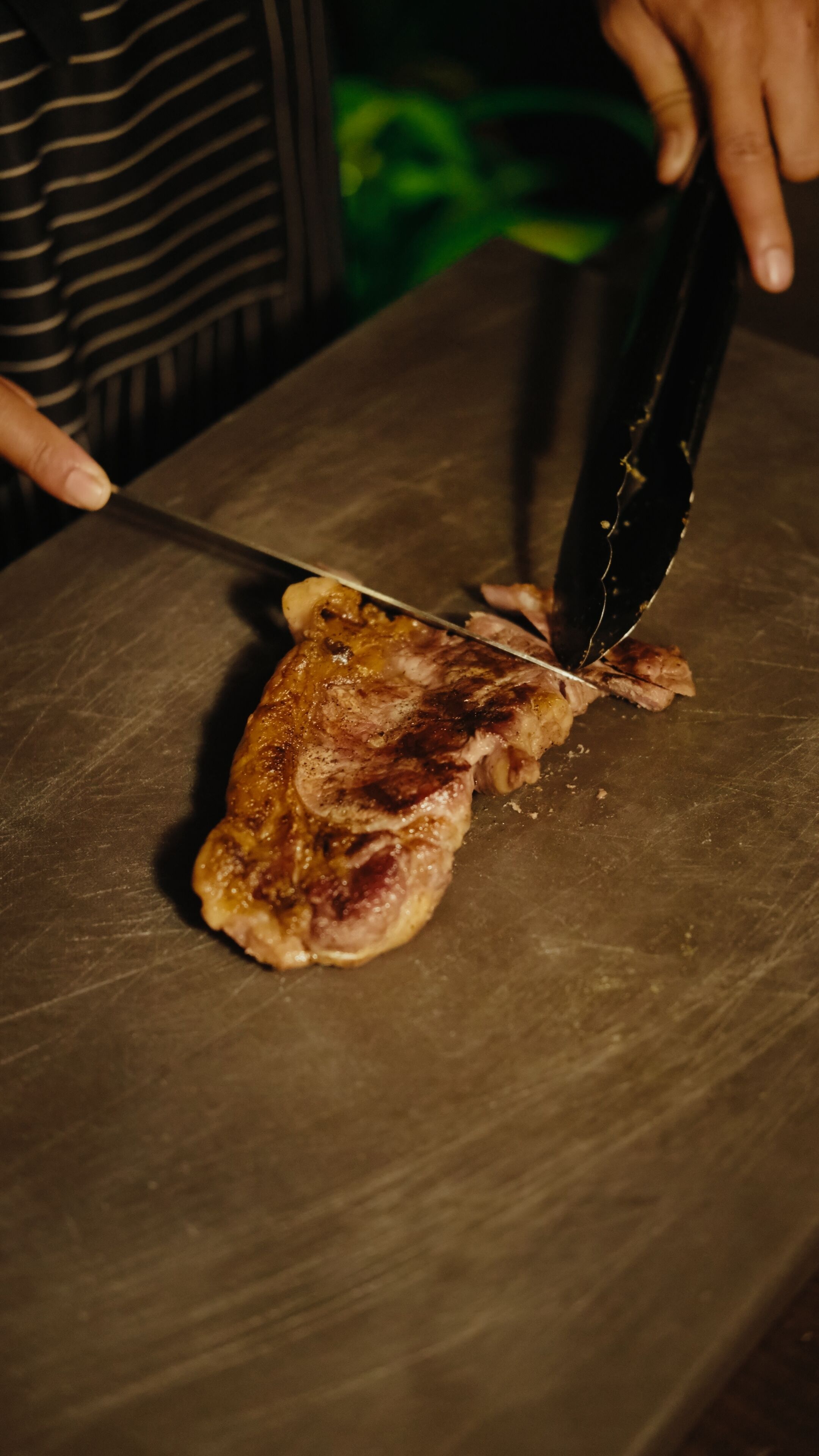 Uma pessoa cortando um pedaço de carne em uma tábua.