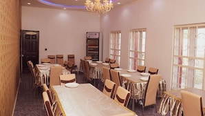 Uma área de refeições com mesas e cadeiras redondas, um candelabro e uma placa indicando a cozinha.